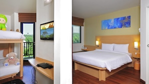 Quarto de hotel com uma cama beliche, uma mesa com um laptop, um urso de pelúcia, uma televisão e um quadro na parede.