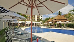 Uma área à beira da piscina com espreguiçadeiras, guarda-sóis e piscina.