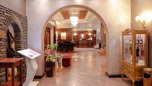 Um saguão de hotel com parede de pedra, balcão de recepção, lustre e uma vitrine.