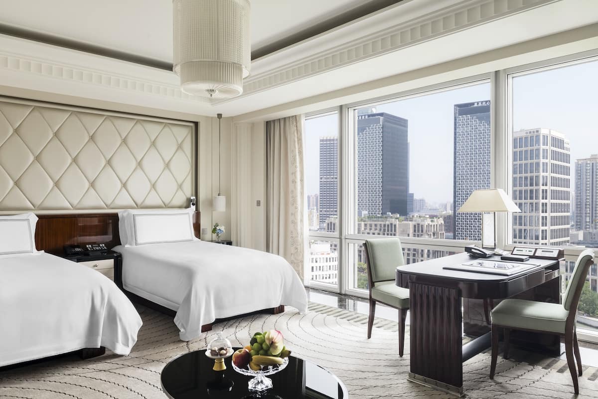 Quarto de hotel com duas camas, uma escrivaninha e vista para a cidade.