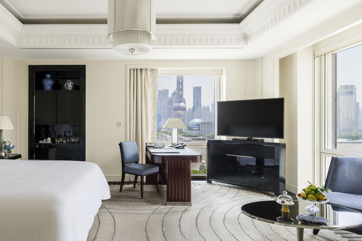 Quarto de hotel com uma cama grande, uma escrivaninha com cadeira, televisão e vista para a cidade.