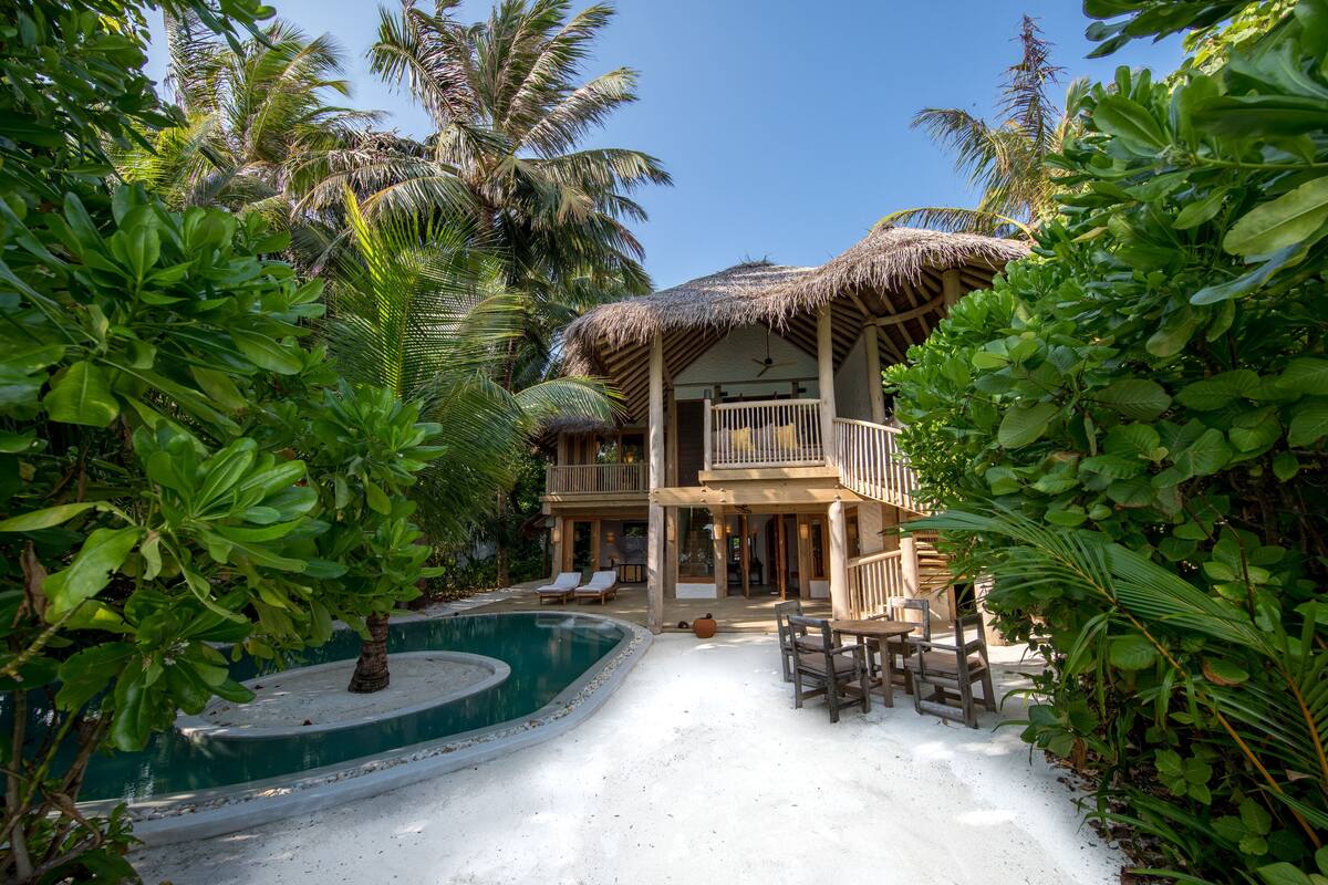 Resort com piscina, espreguiçadeiras e uma estrutura com telhado de palha.