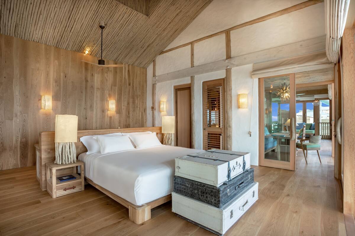 Quarto com piso de madeira, uma cama, abajures e uma pilha de malas.