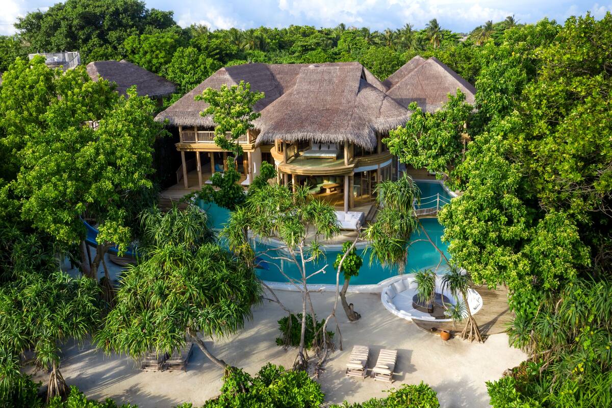 Resort com villas de telhado de palha, piscina central e exuberante paisagem tropical.