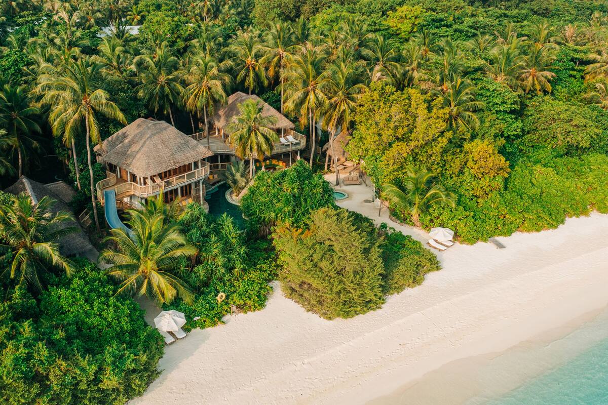 Vista aérea de um resort com um edifício de telhado de palha, piscina e praia.