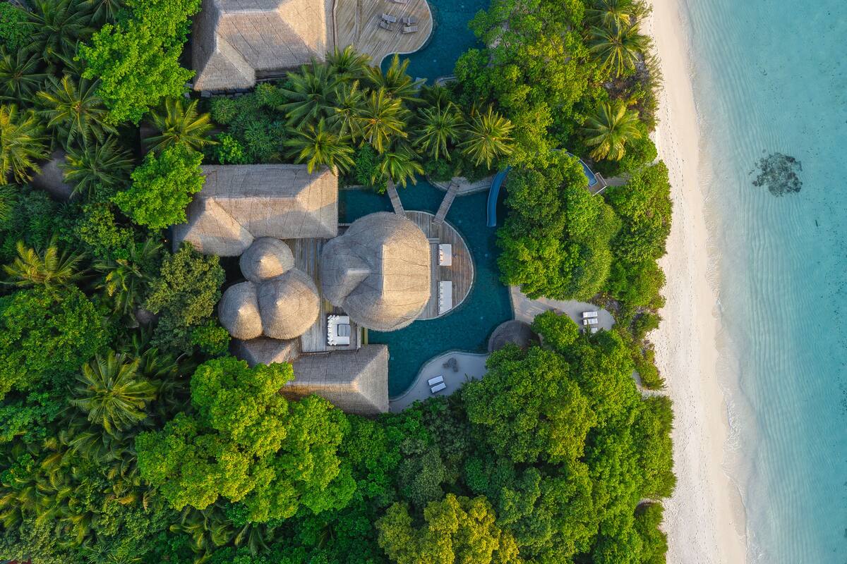 Vista aérea de um resort com piscina, cercado por vegetação exuberante e palmeiras, com vista para uma praia arenosa.