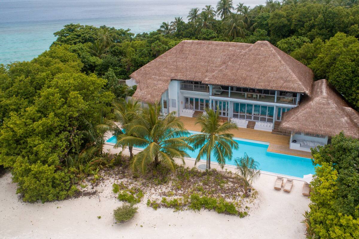 Uma casa grande com telhado de palha, piscina e praia.