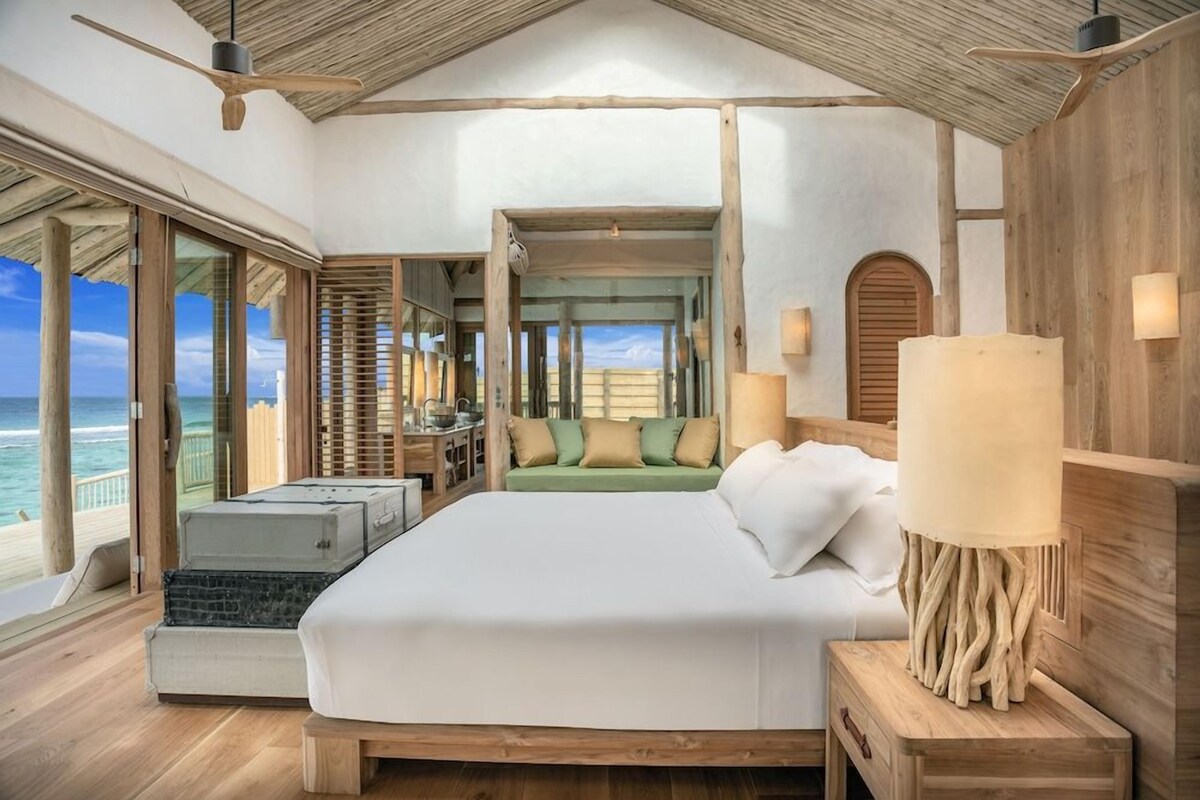 Quarto espaçoso com cama grande, cabeceira de madeira e vista para o oceano.