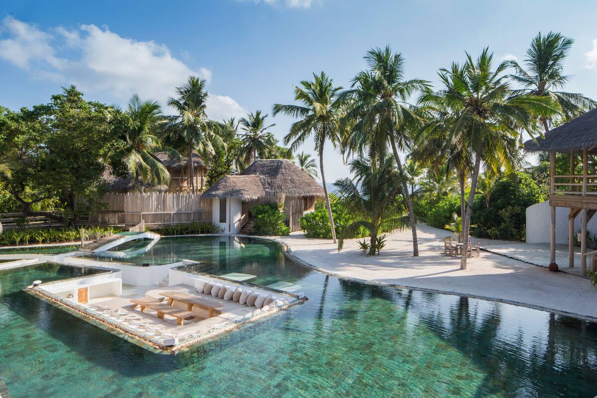 Piscina de resort com água cristalina, espreguiçadeiras e palmeiras.