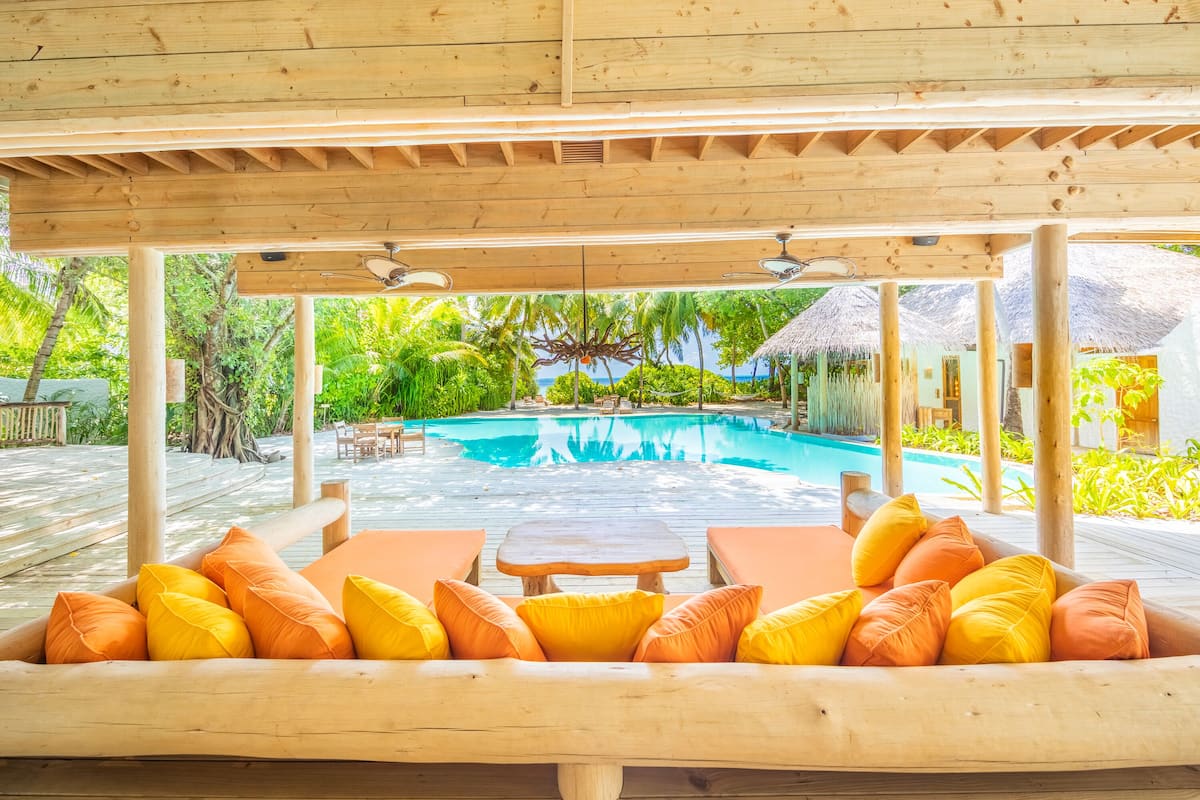 Um deck de madeira com piscina, espreguiçadeiras e uma estrutura com telhado de palha.
