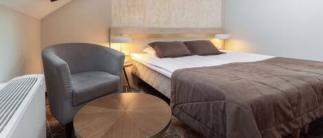 Quarto de hotel com cama, poltrona, mesa redonda e radiador.