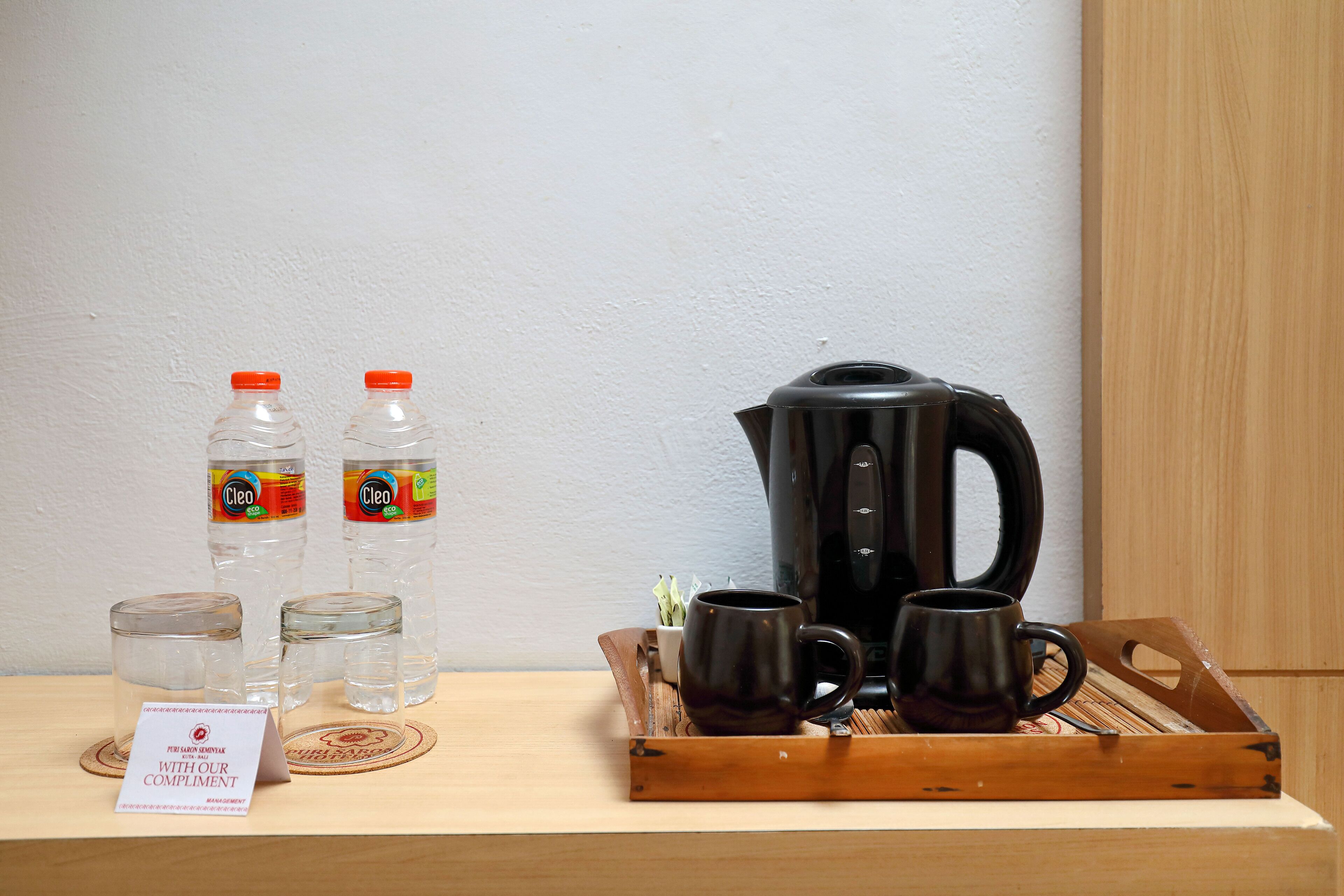 Uma bandeja com uma cafeteira de café preto, duas canecas pretas e duas garrafas transparentes com tampas laranja sobre uma superfície de madeira.