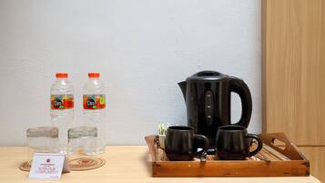 Uma bandeja com uma cafeteira de café preto, duas canecas pretas e duas garrafas transparentes com tampas laranja sobre uma superfície de madeira.