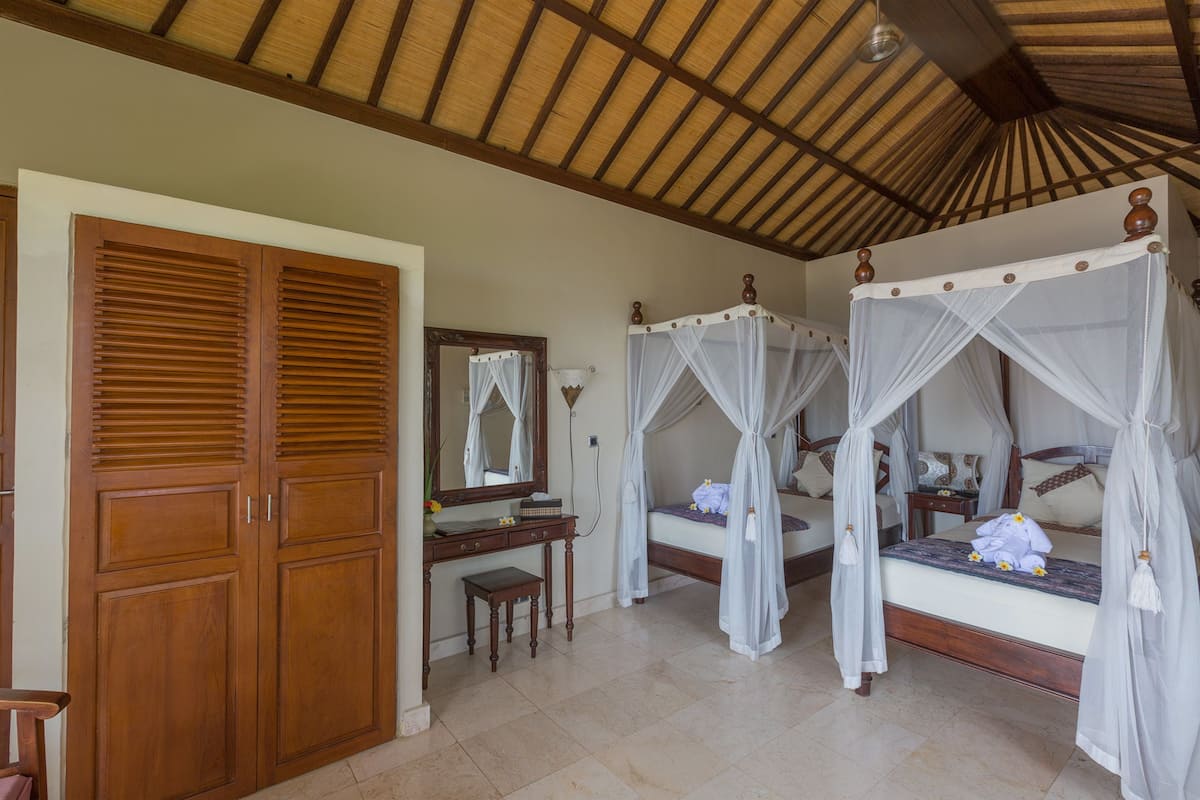 Quarto com guarda-roupa de madeira, penteadeira com espelho e duas camas de dossel com cortinas.
