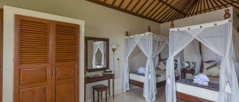 Quarto com guarda-roupa de madeira, penteadeira com espelho e duas camas de dossel com cortinas.