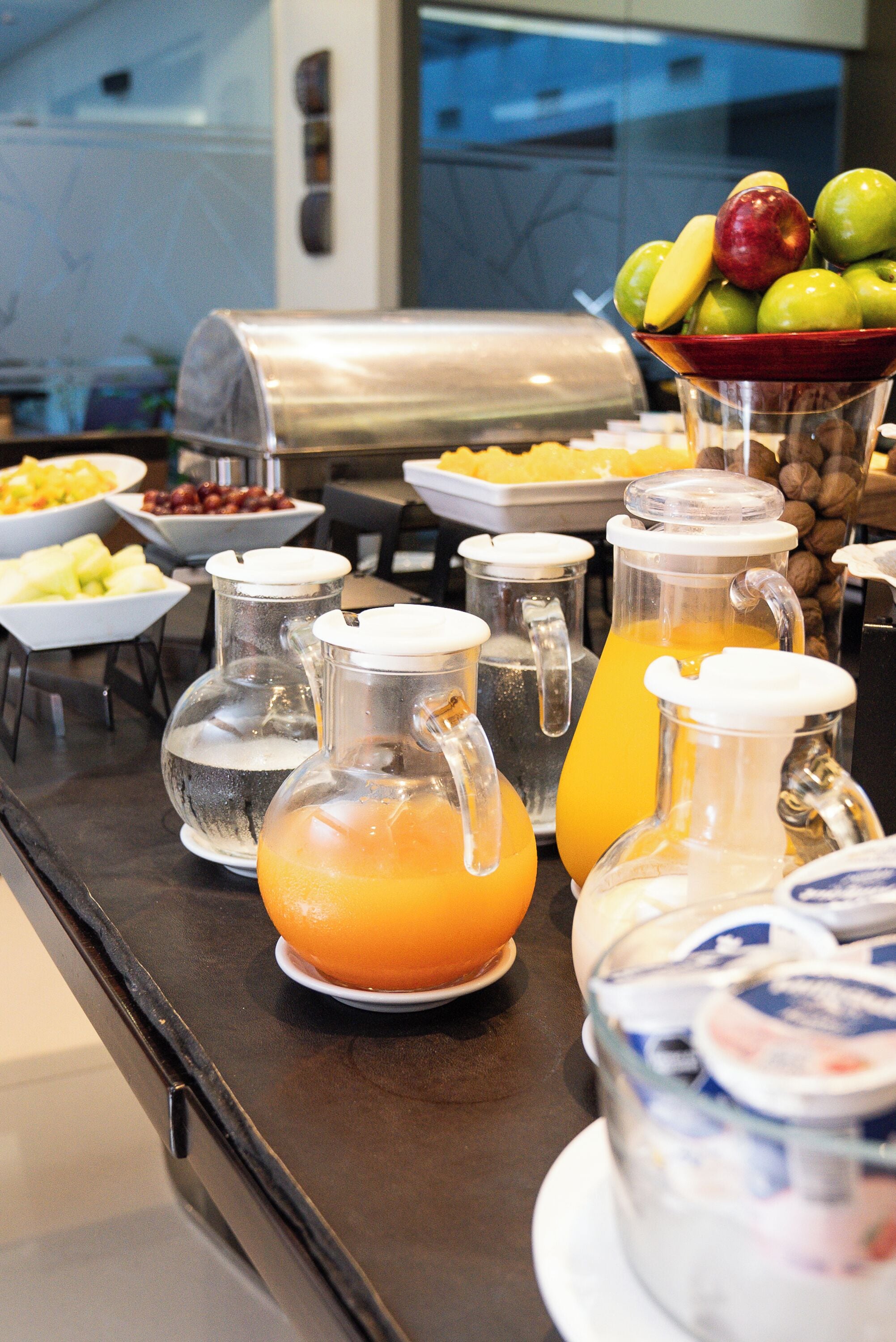 Buffet com diversas opções de comida e bebida, incluindo frutas, sucos e produtos lácteos.