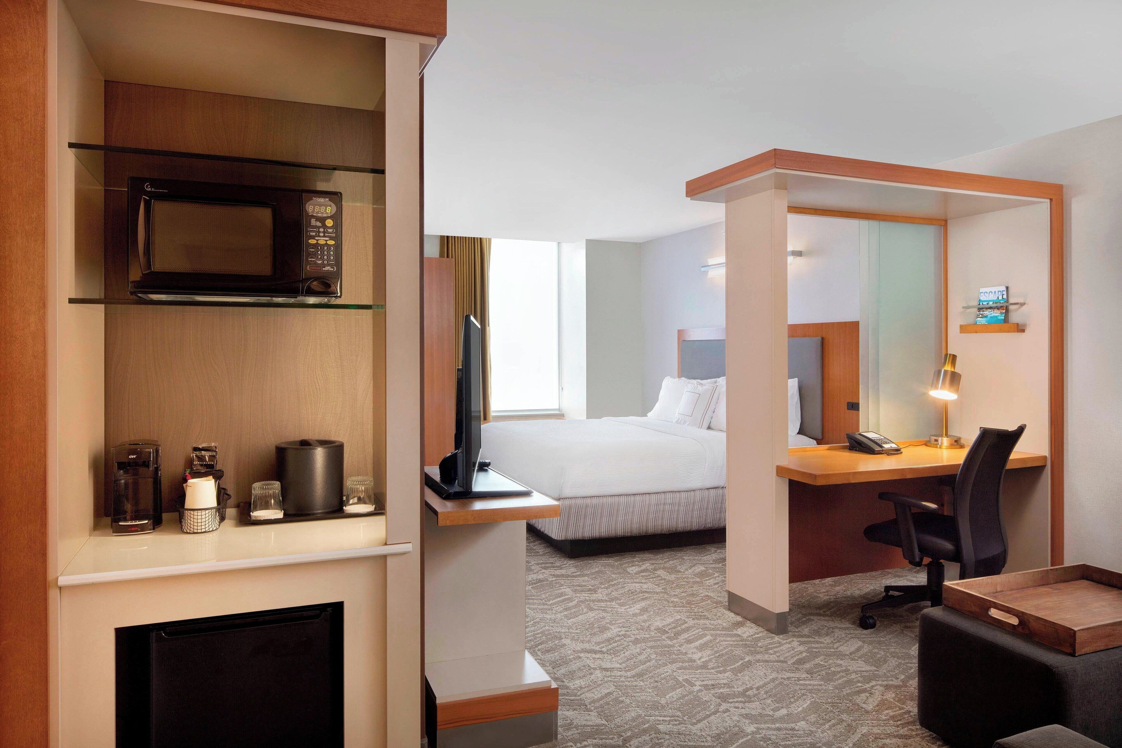 Quarto de hotel com cama, escrivaninha com computador, micro-ondas e televisão.