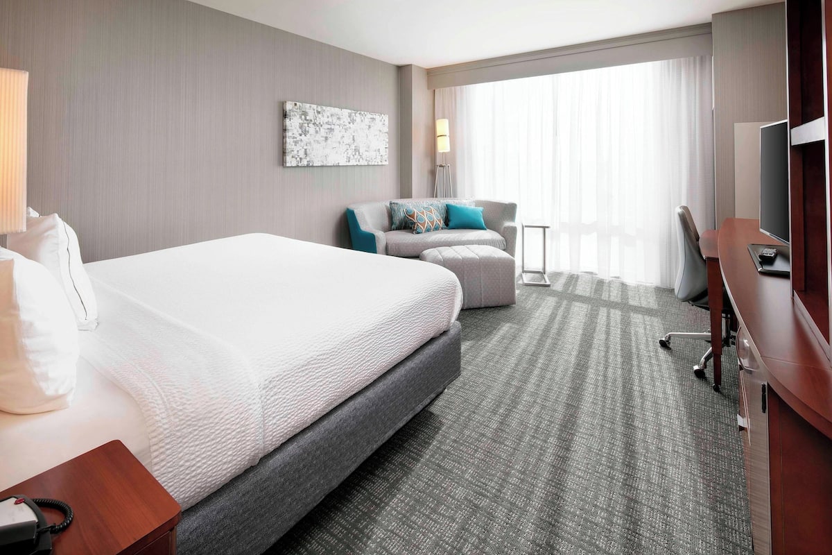 Quarto de hotel com uma cama grande, uma escrivaninha com cadeira, um sofá e uma televisão.