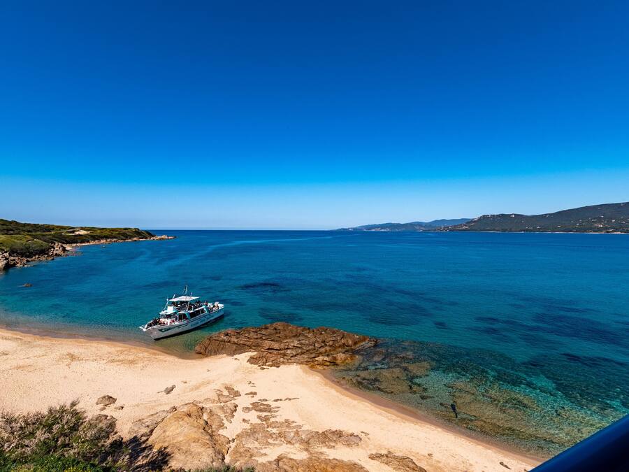 Vista costeira com barco perto de uma praia arenosa e formações rochosas.