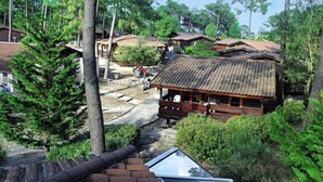 Um edifício tradicional japonês com telhado de telhas, rodeado por vegetação densa e outras construções residenciais.