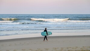 Uma pessoa caminhando na praia segurando uma prancha de surf.