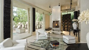 Uma sala de estar moderna com uma mesa de centro de vidro, sofás brancos, lareira e vista para o exterior.