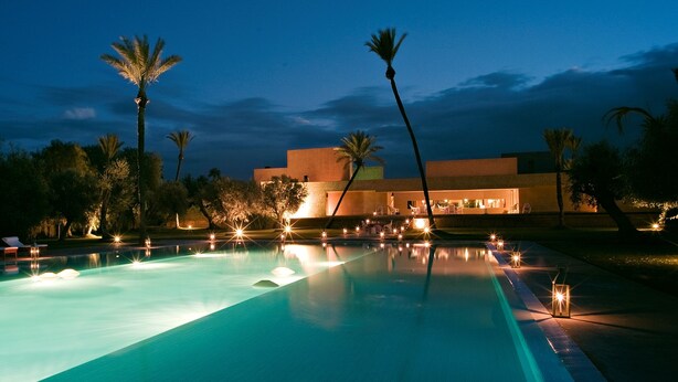 Piscina com vista para um edifício e palmeiras ao entardecer.