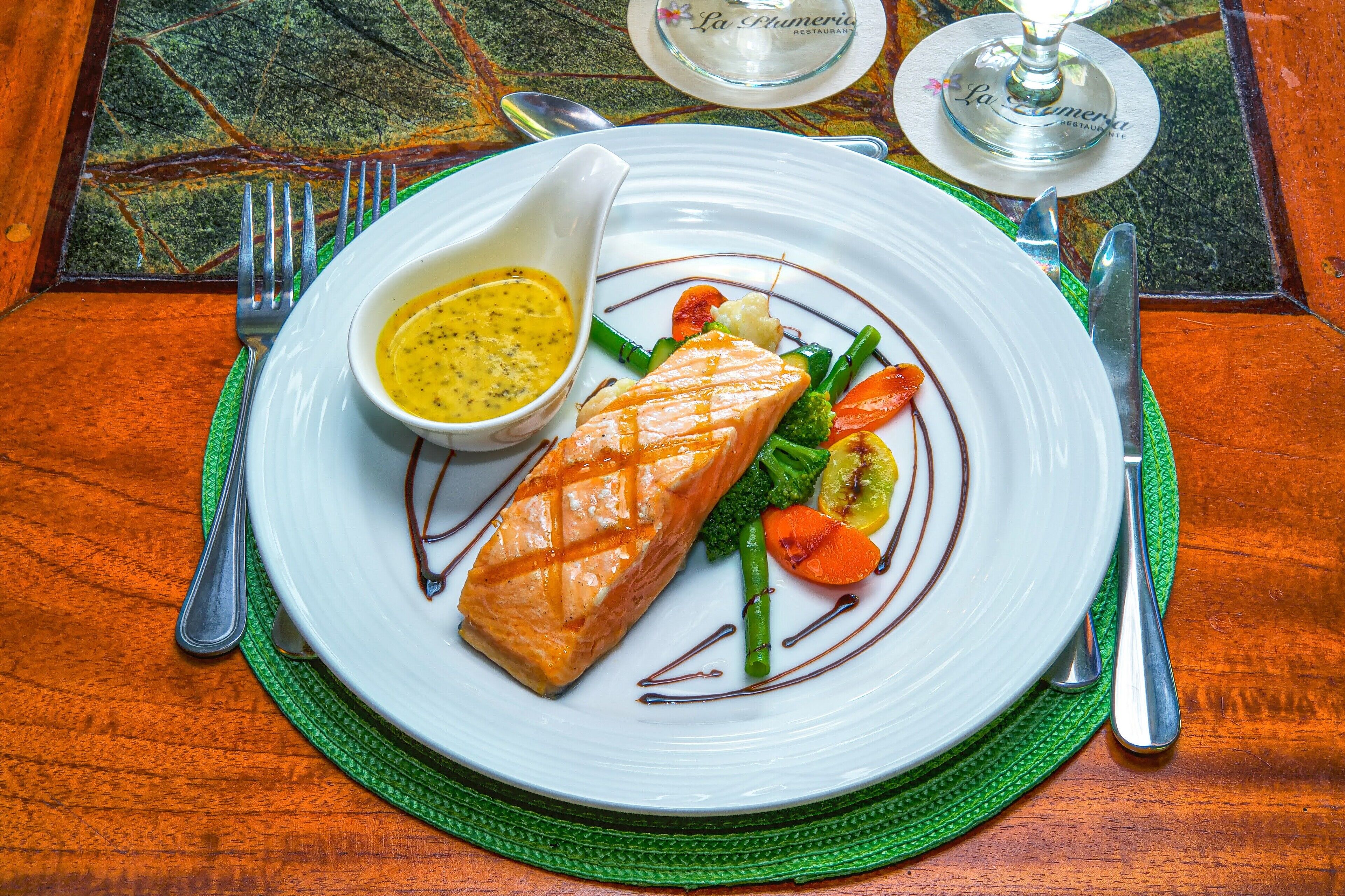Prato de comida com salmão, legumes e molho sobre uma mesa com jogo americano.