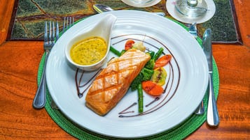 Prato de comida com salmão, legumes e molho sobre uma mesa com jogo americano.
