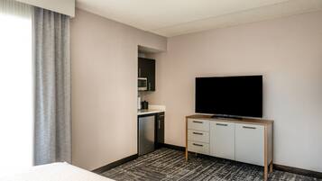 Quarto de hotel com cama, televisão de tela plana, pequeno espaço de cozinha e piso coberto de carpete.