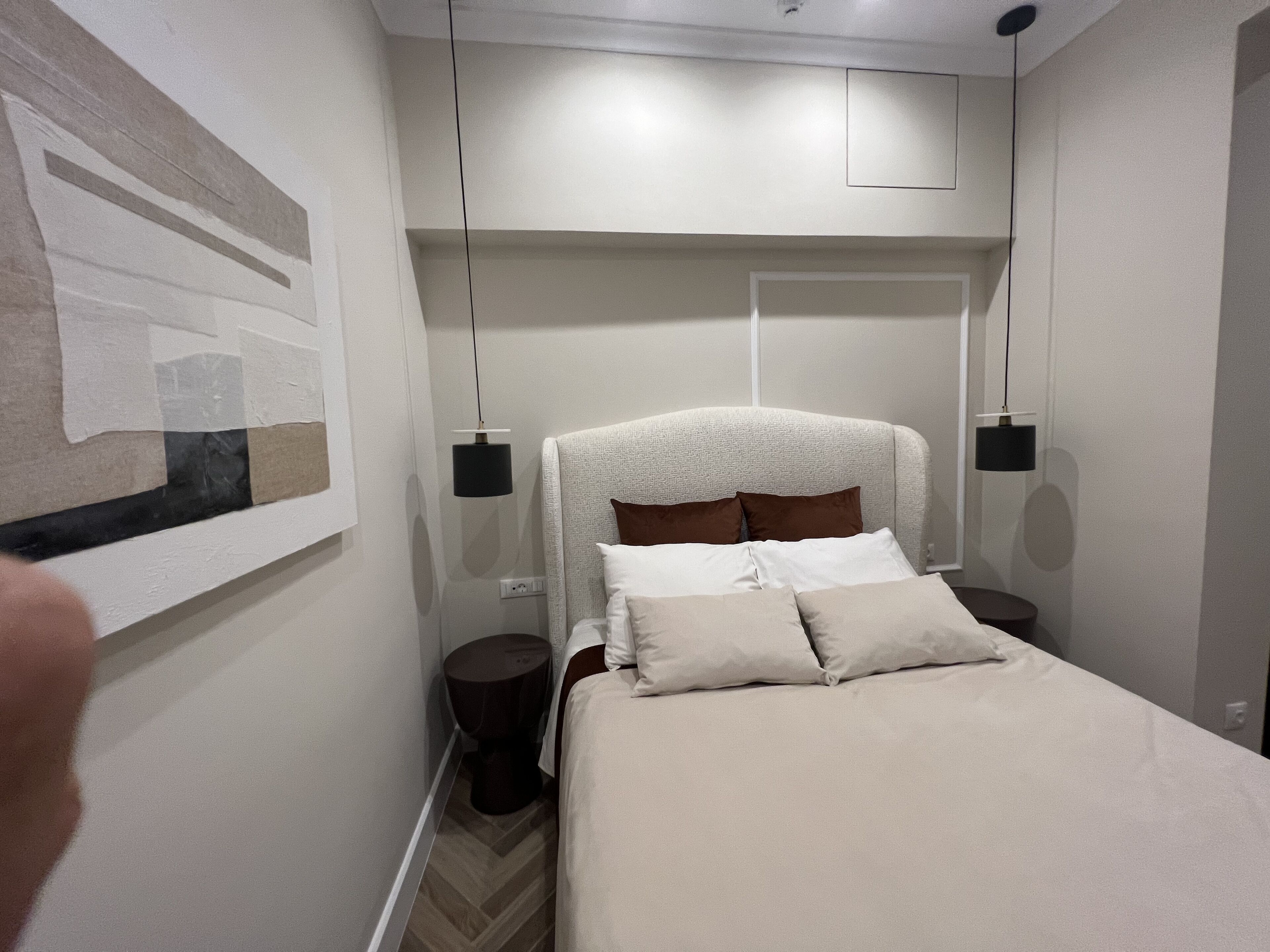 Quarto com cama, duas mesas de cabeceira, luminária na parede e um quadro.