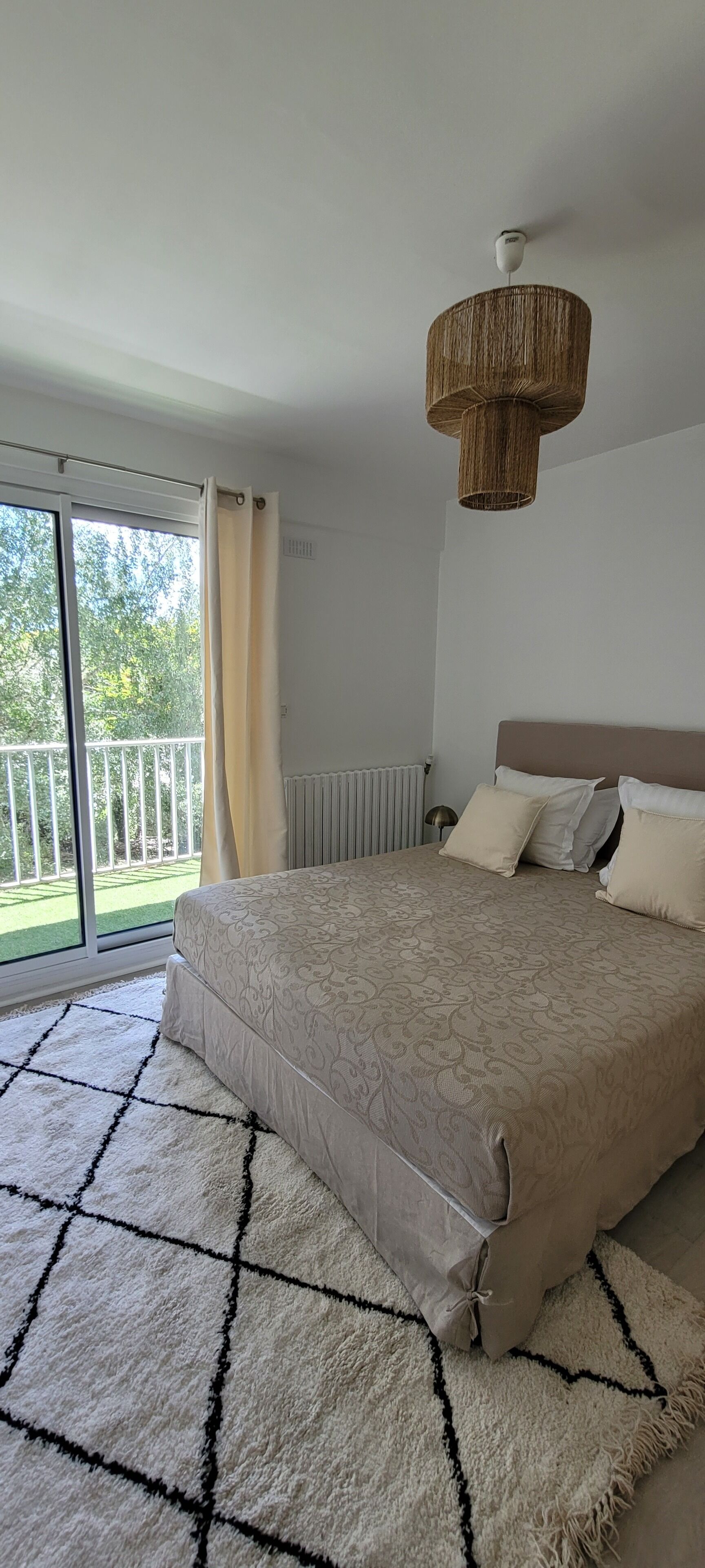 Quarto com uma cama grande, ventoinha no teto e vista para uma varanda com vegetação.