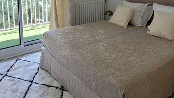 Quarto com uma cama grande, ventoinha no teto e vista para uma varanda com vegetação.