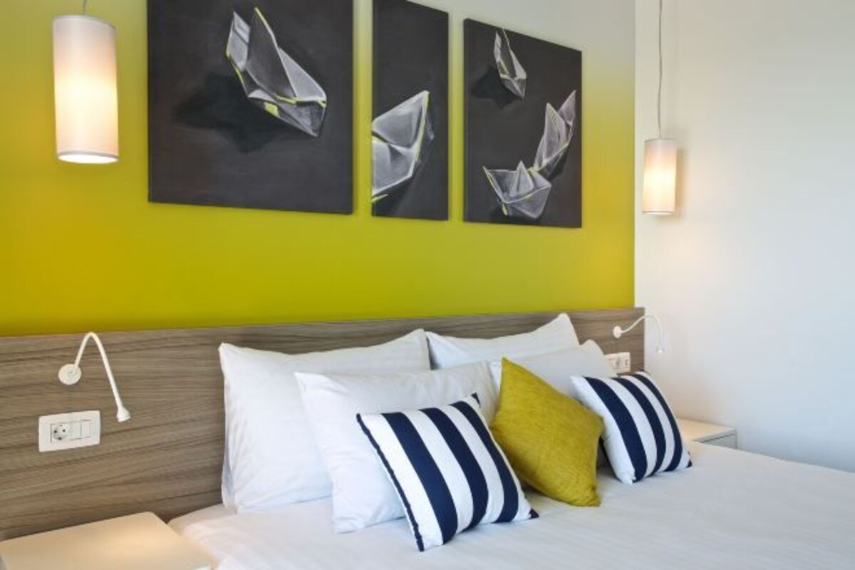 Quarto de hotel com cama, almofadas, cabeceira e obras de arte na parede.