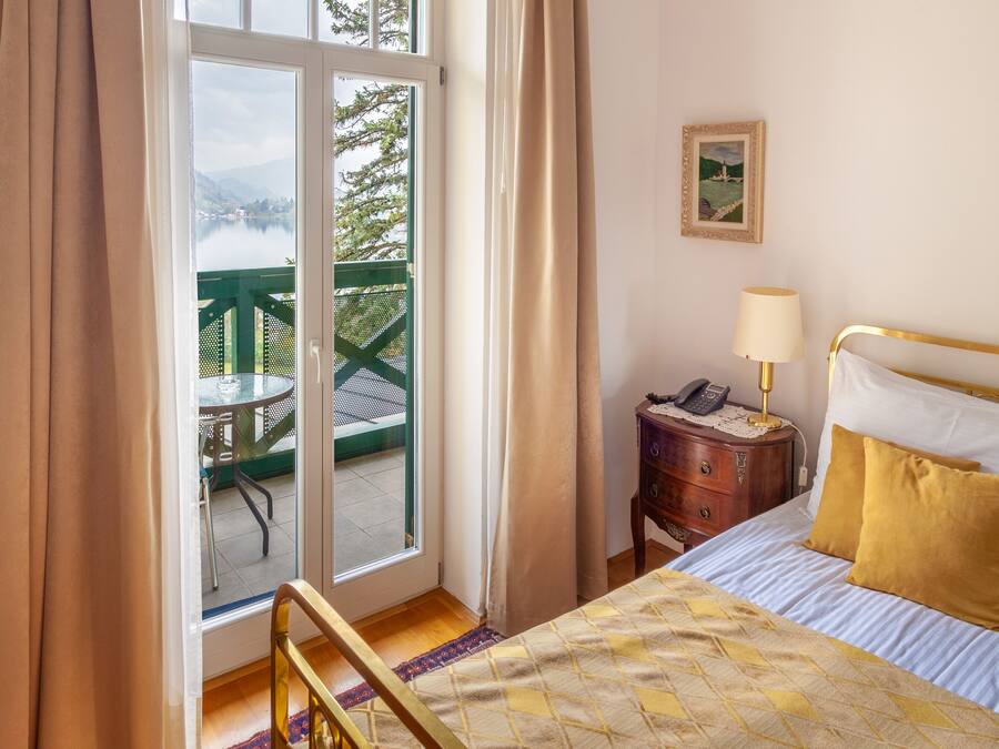 Quarto com cama, mesa de cabeceira, luminária, quadro na parede e varanda com mesa e cadeiras.