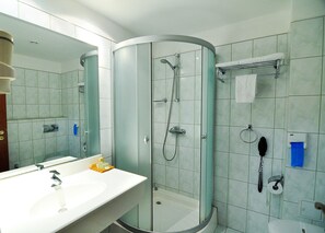 Um banheiro com pia branca, chuveiro com box de vidro e porta-toalhas.