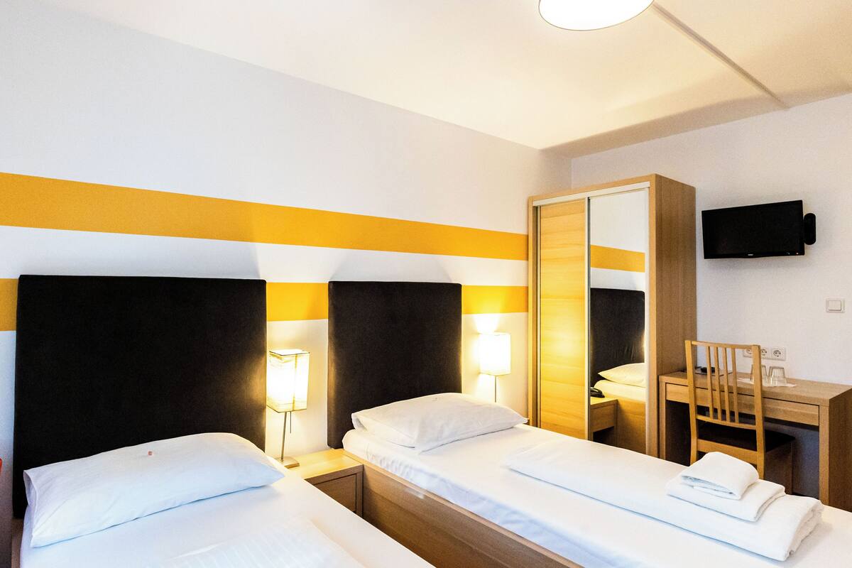 Quarto de hotel com duas camas, uma escrivaninha, uma cadeira, uma televisão e um espelho.