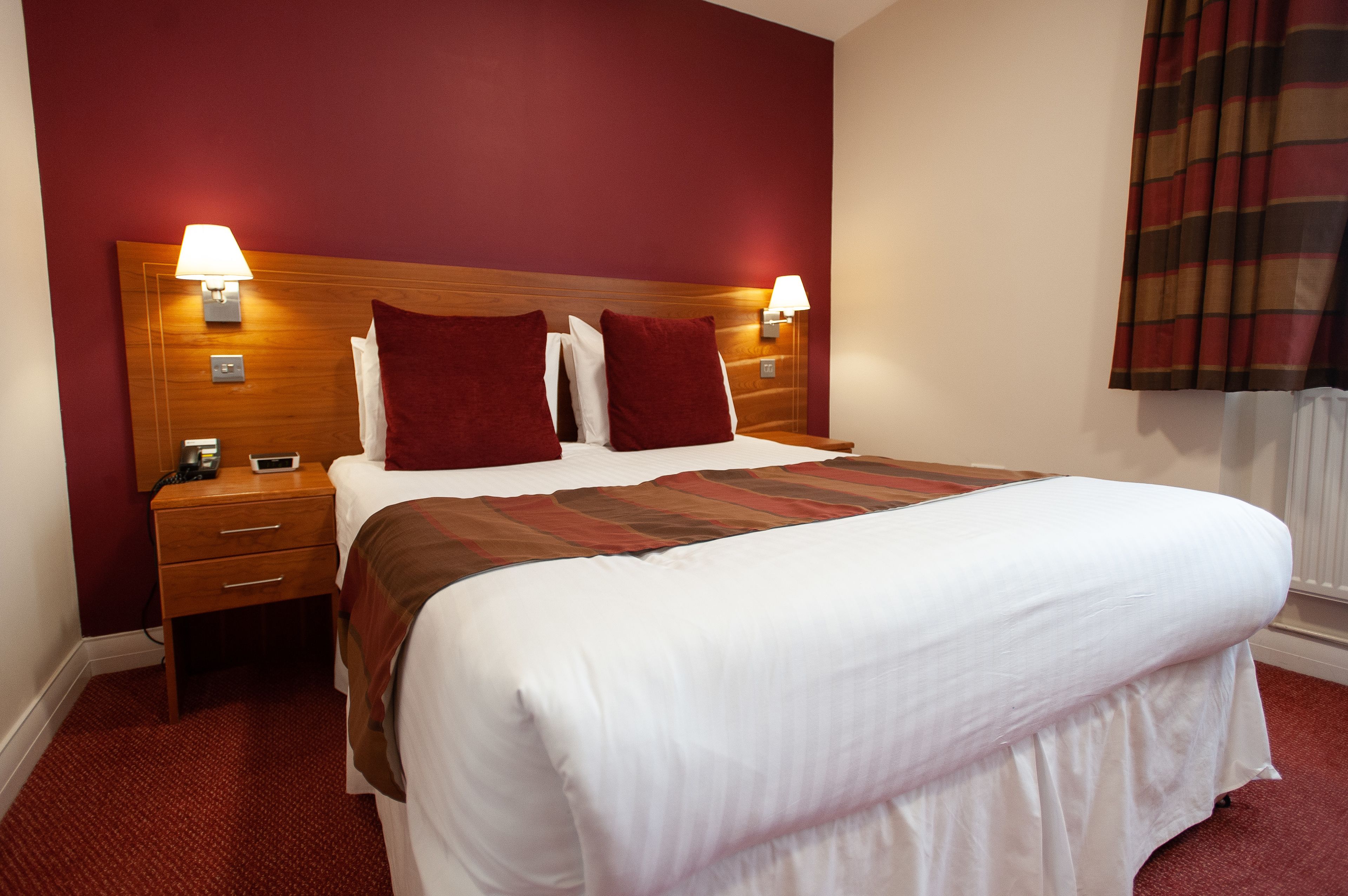 Quarto de hotel com uma cama grande, duas mesas de cabeceira e cabeceira com iluminação embutida.