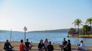Um grupo de pessoas meditando em um cais de madeira à beira de um lago.