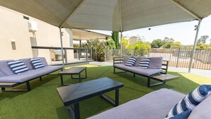 Uma área de pátio ao ar livre com dois sofás e uma mesa, rodeada por um espaço de estar coberto.