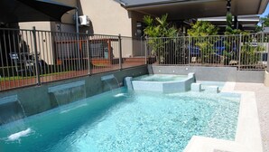 Piscina com hidromassagem, cercada por uma grade e um espaço de área coberta.