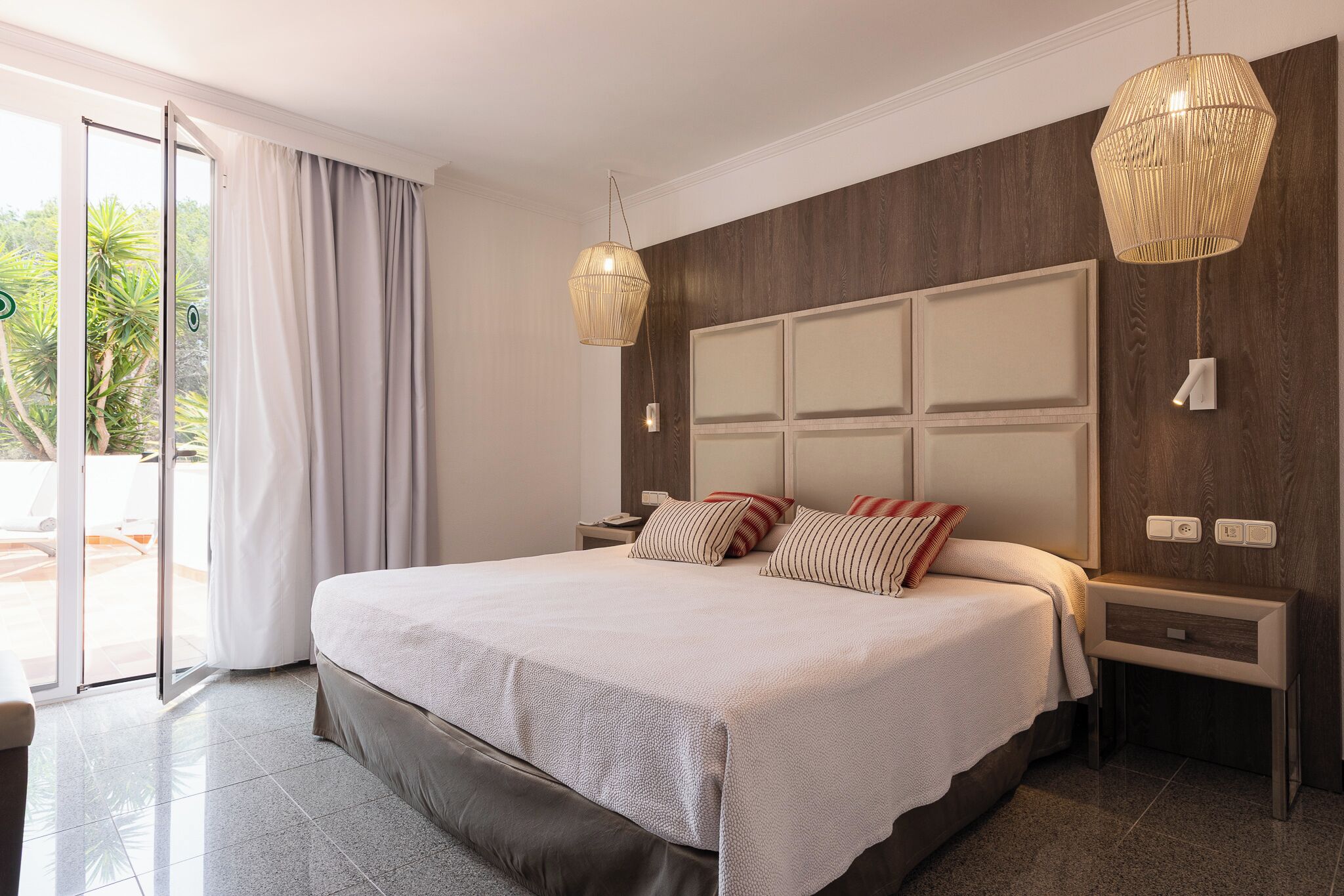 Quarto moderno com uma cama grande, cabeceira de madeira, mesa de cabeceira e luminária pendente.