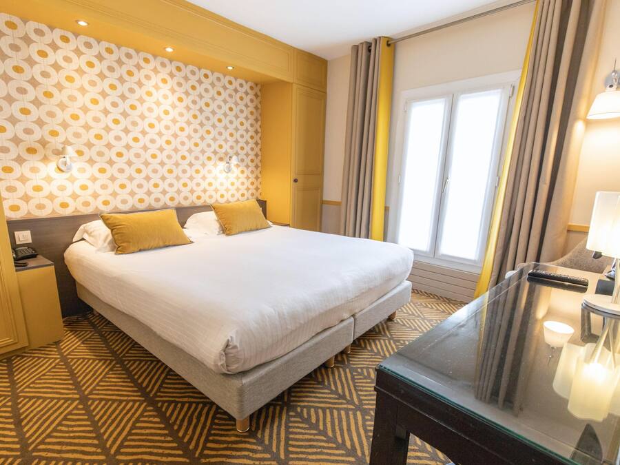 Quarto de hotel com uma cama grande, mesa de cabeceira, espelho e parede estampada.