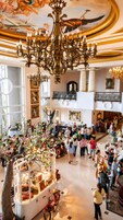Um hall imponente com um grande candelabro, vários andares e um arranjo floral central.