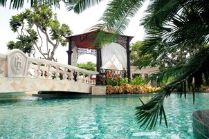 Área de piscina com uma ponte, um gazebo e palmeiras.