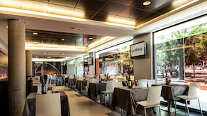 Um restaurante moderno com mesas preparadas para refeições, uma grande janela com vista para o exterior, e um letreiro com a inscrição "LA GRADA".