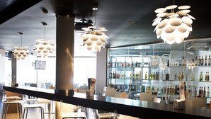 Uma área de bar com um balcão comprido, várias luminárias pendentes e um expositor de garrafas de vidro.