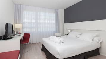 Quarto de hotel com uma cama, uma escrivaninha com computador, uma cadeira e uma televisão.