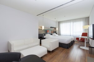 Quarto de hotel moderno com uma cama grande, um sofá, uma escrivaninha e uma televisão.