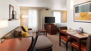 Quarto de hotel com sofá, televisão, mesa de jantar e uma pintura grande na parede.